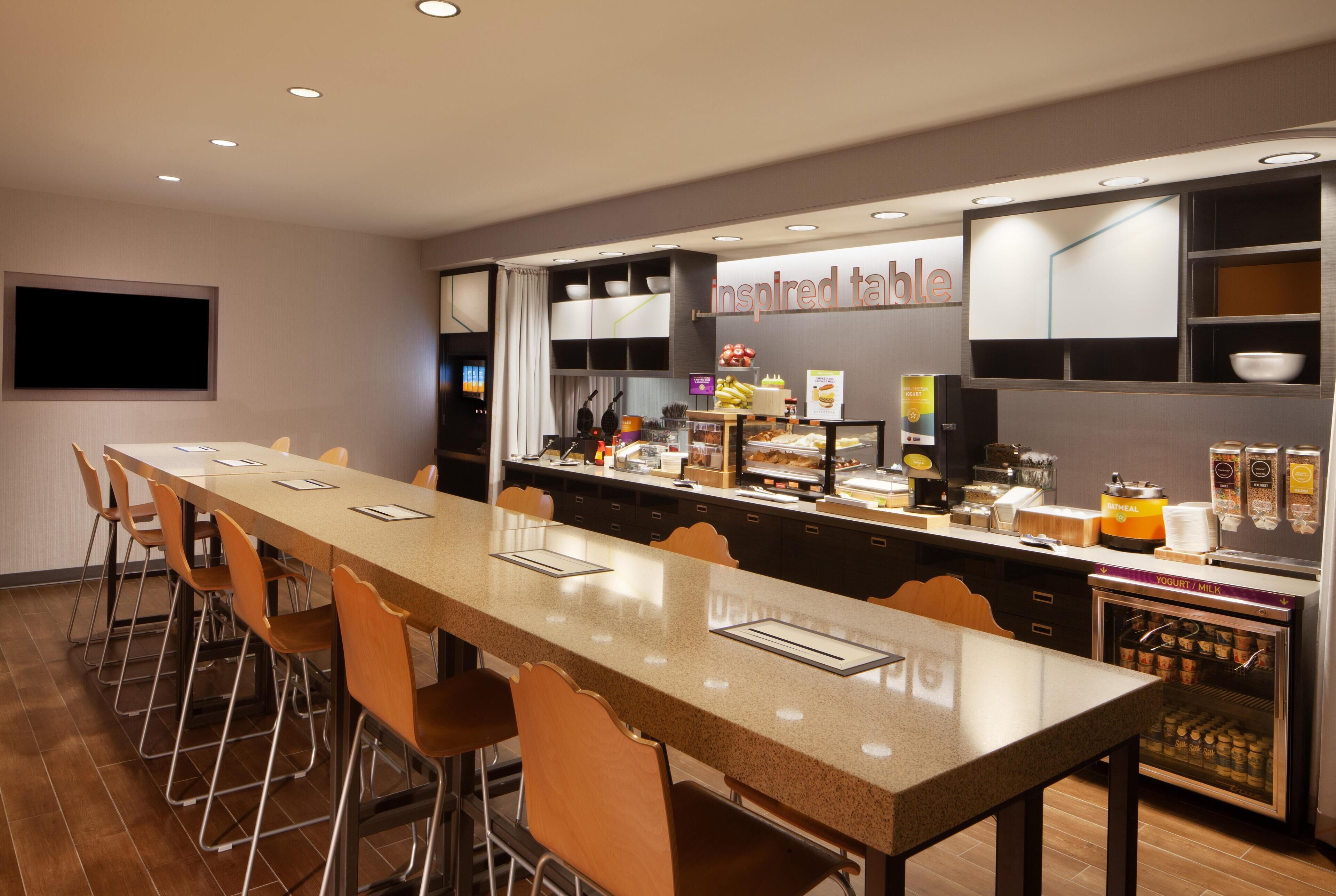 Uma cozinha moderna com um balcão extenso, banquetas e uma geladeira abastecida com bebidas.