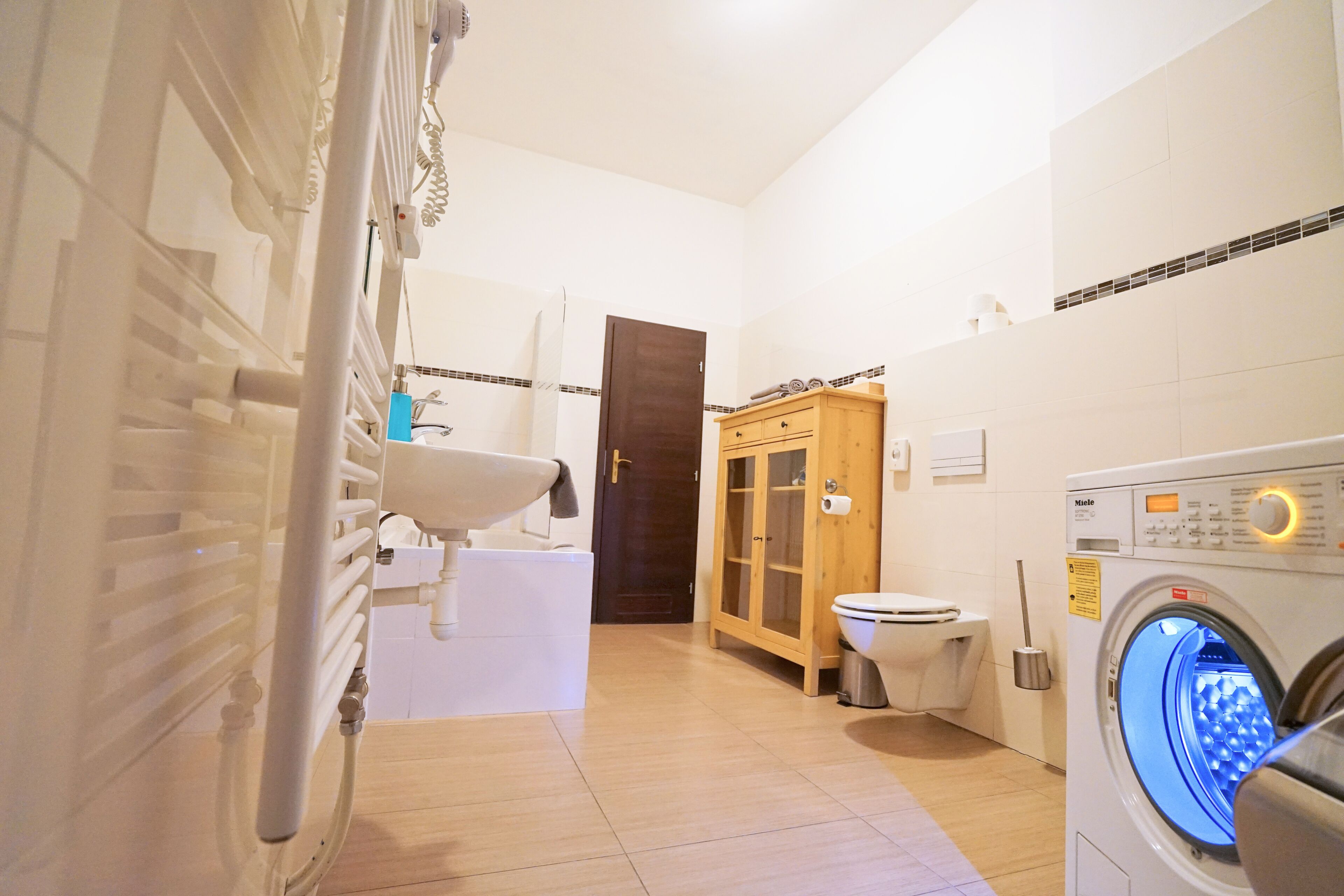 Um banheiro moderno com radiador embutido, armário de madeira, vaso sanitário e máquina de lavar com abertura frontal.