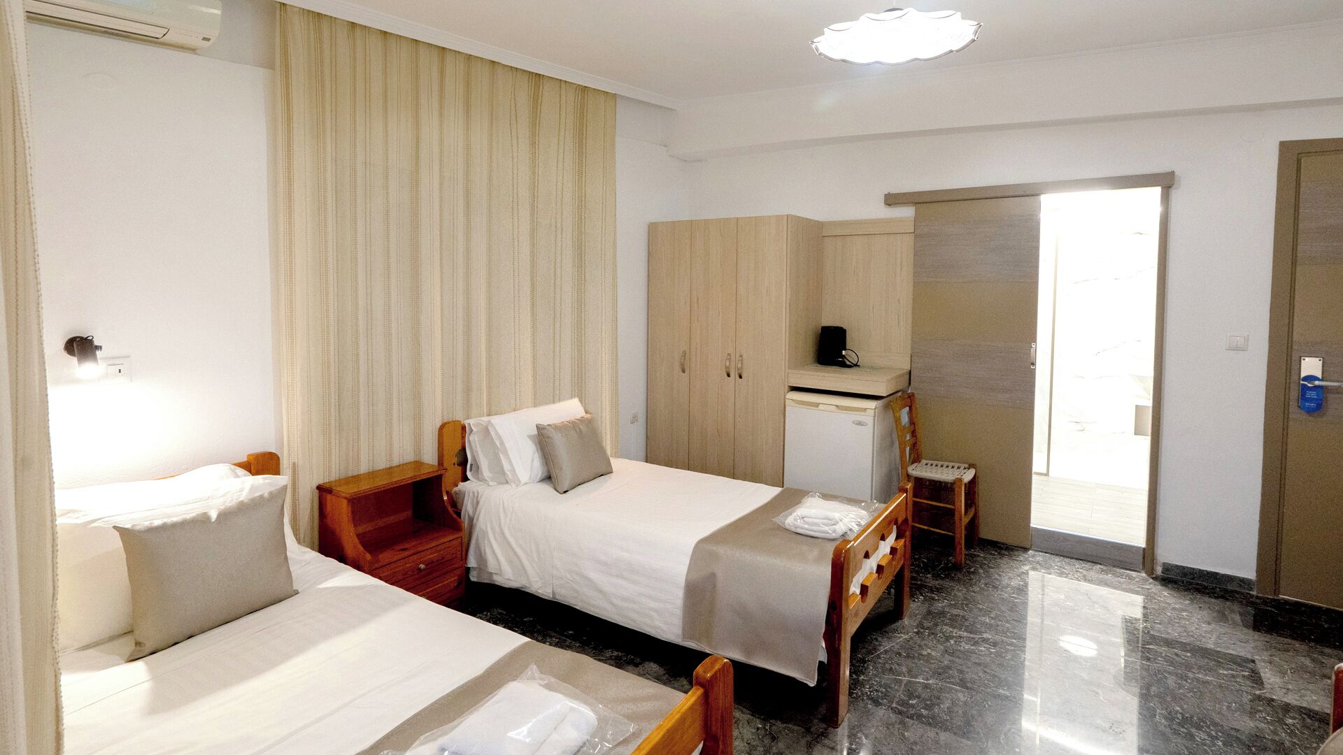 Quarto de hotel com duas camas, um guarda-roupa, uma escrivaninha e um espelho.