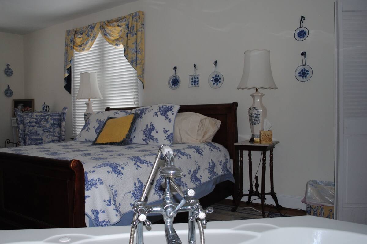 Quarto com cama grande, mesa de cabeceira com abajur, banheiro com banheira e detalhes decorativos nas paredes.