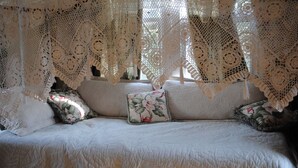 Uma cama com travesseiro floral e manta acolchoada, um baldaquim de renda e uma janela com cortinas.