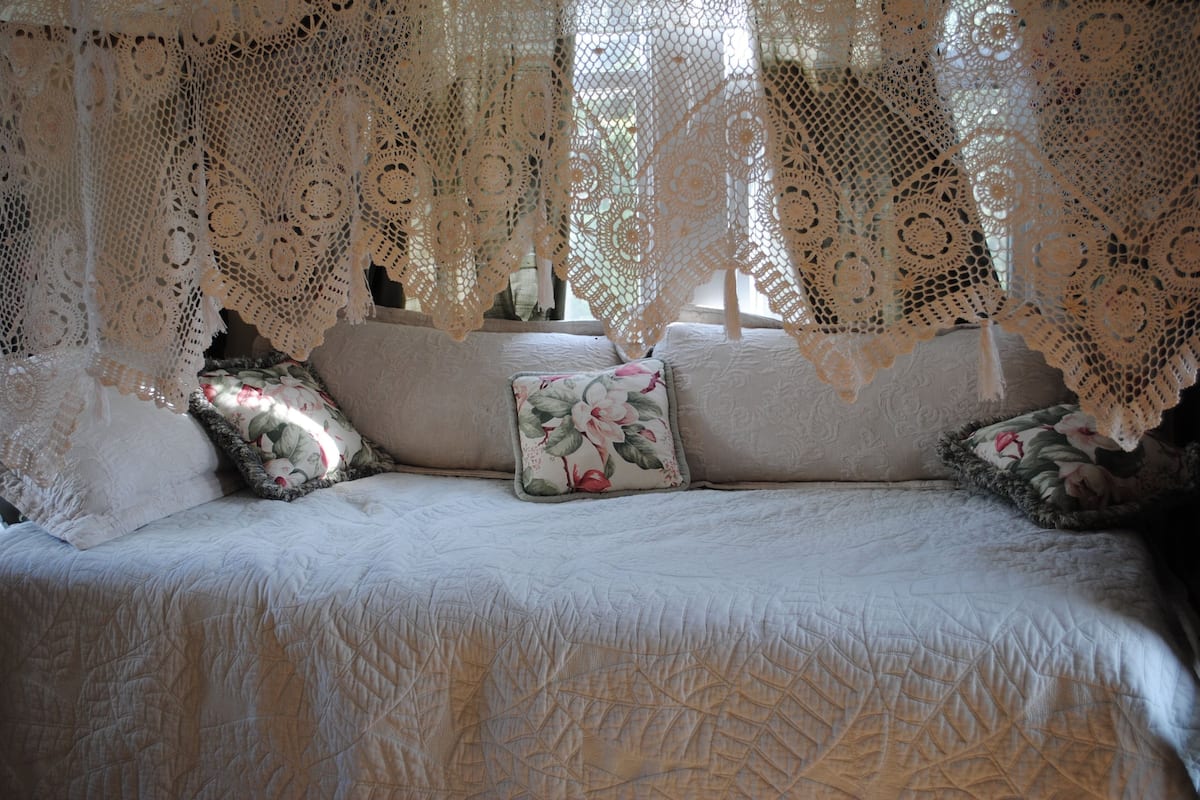 Uma cama com travesseiro floral e manta acolchoada, um baldaquim de renda e uma janela com cortinas.