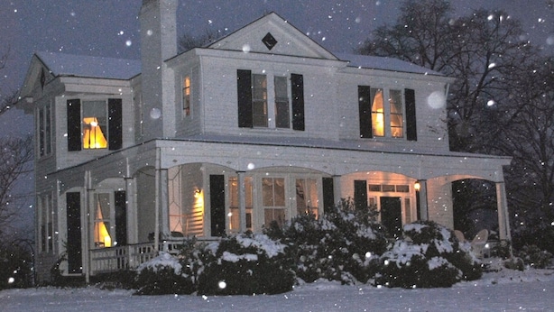 Uma casa de dois andares com entrada central, várias janelas e chaminé. Neve cai lá fora.