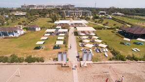 Vista aérea de um resort à beira-mar com espreguiçadeiras, guarda-sóis e quadra de vôlei.