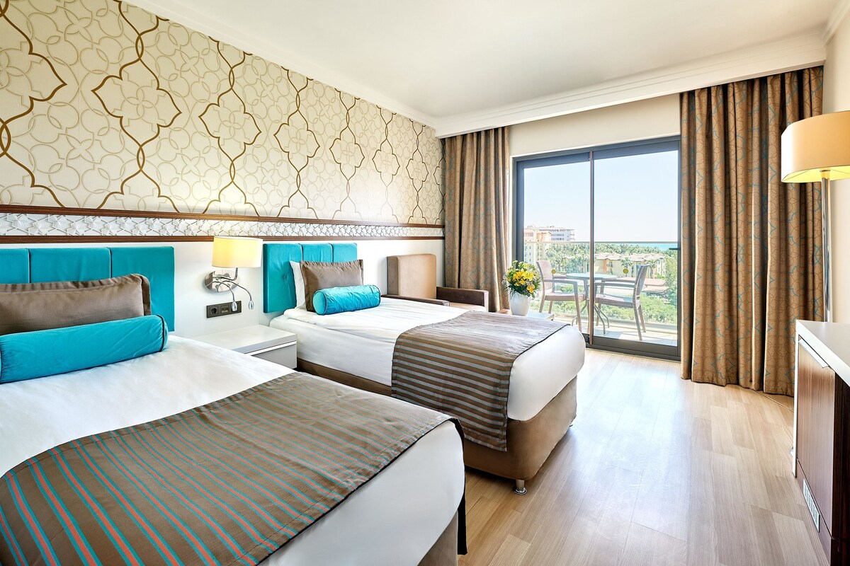 Quarto de hotel com duas camas, uma janela grande com cortinas e vista para a cidade, e design moderno.