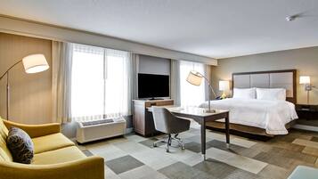 Quarto de hotel com cama, escrivaninha, cadeira, televisão e ar condicionado.
