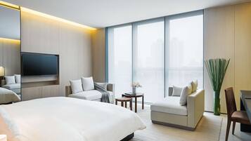 Quarto de hotel moderno com uma cama grande, um sofá, uma escrivaninha e uma televisão na parede.
