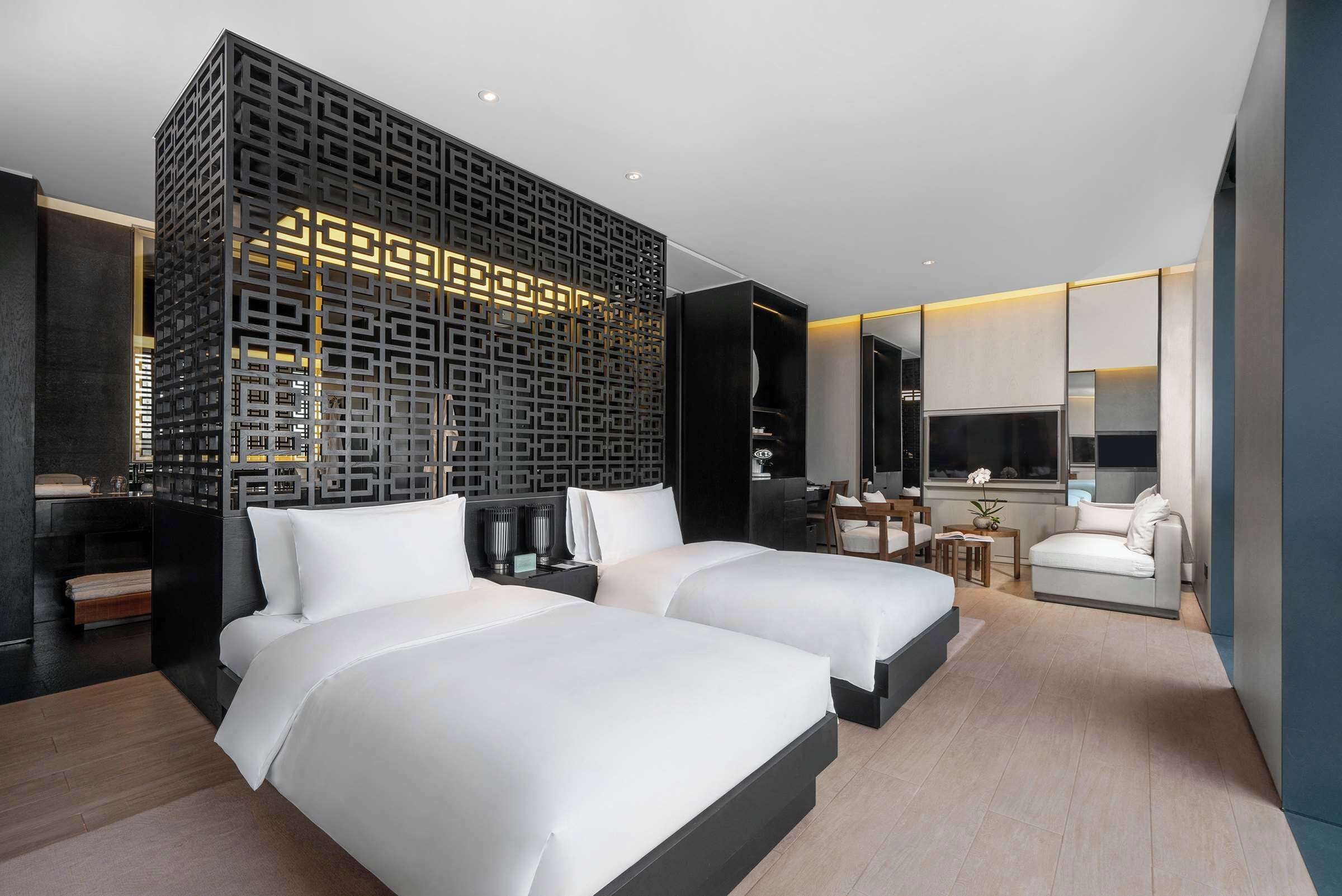 Quarto de hotel moderno com duas camas, um painel decorativo, uma área de estar e uma janela grande.
