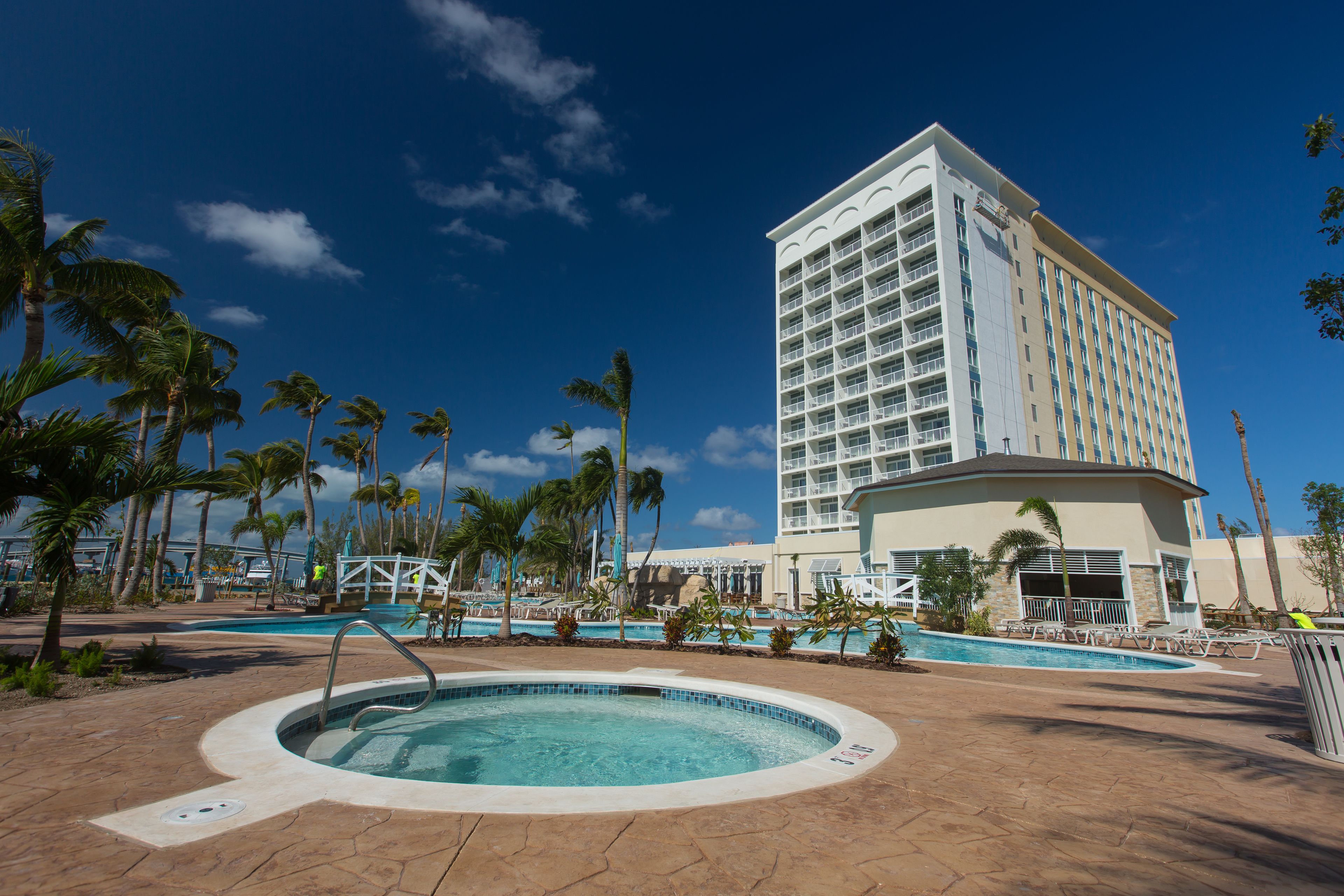 Um hotel com uma grande área de piscina, palmeiras e um edifício moderno com varandas.