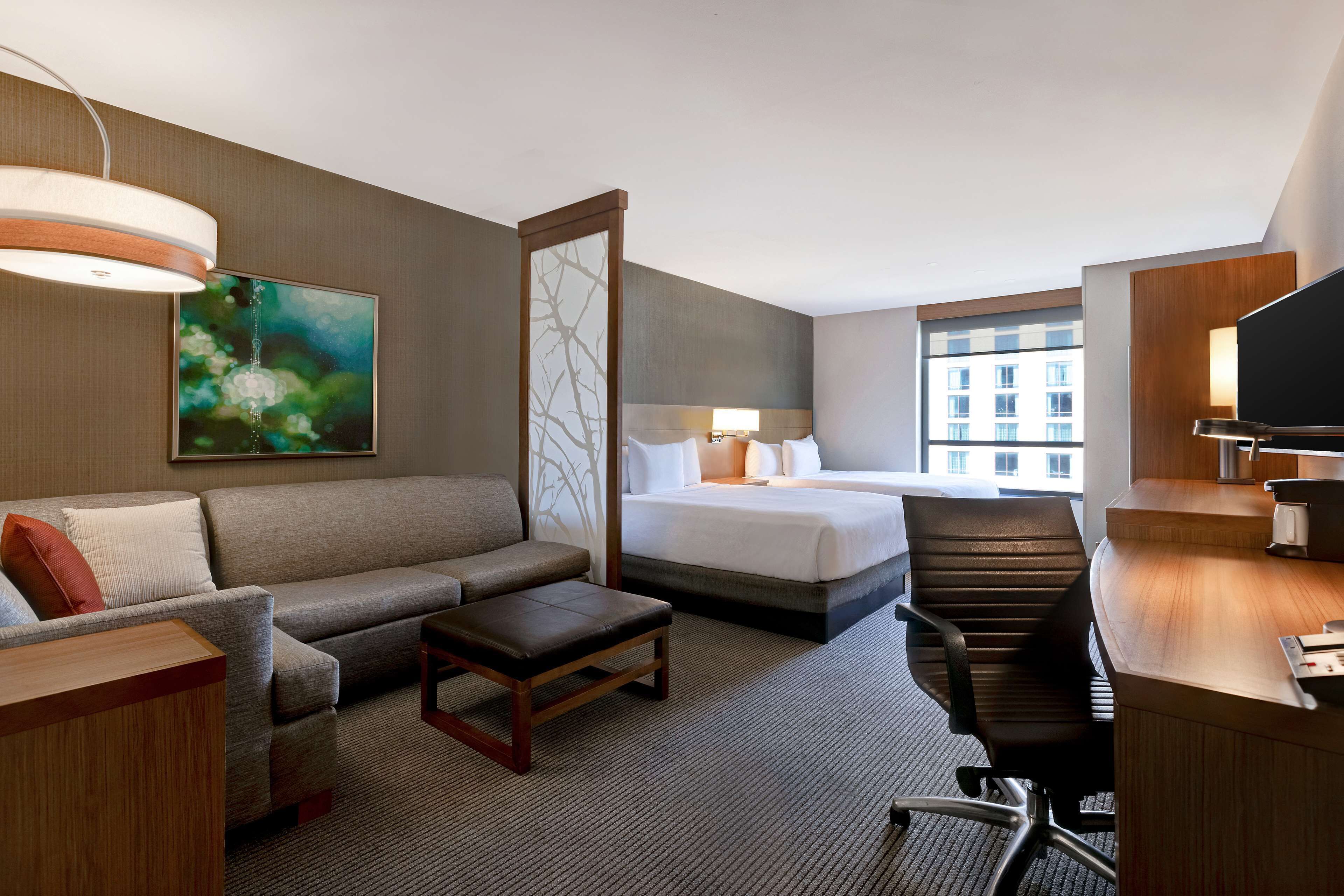 Quarto de hotel com cama, sofá, escrivaninha e televisão.