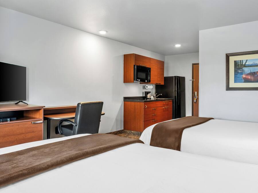 Quarto de hotel com cama, escrivaninha com cadeira, televisão, micro-ondas, frigorífico e um quadro na parede.