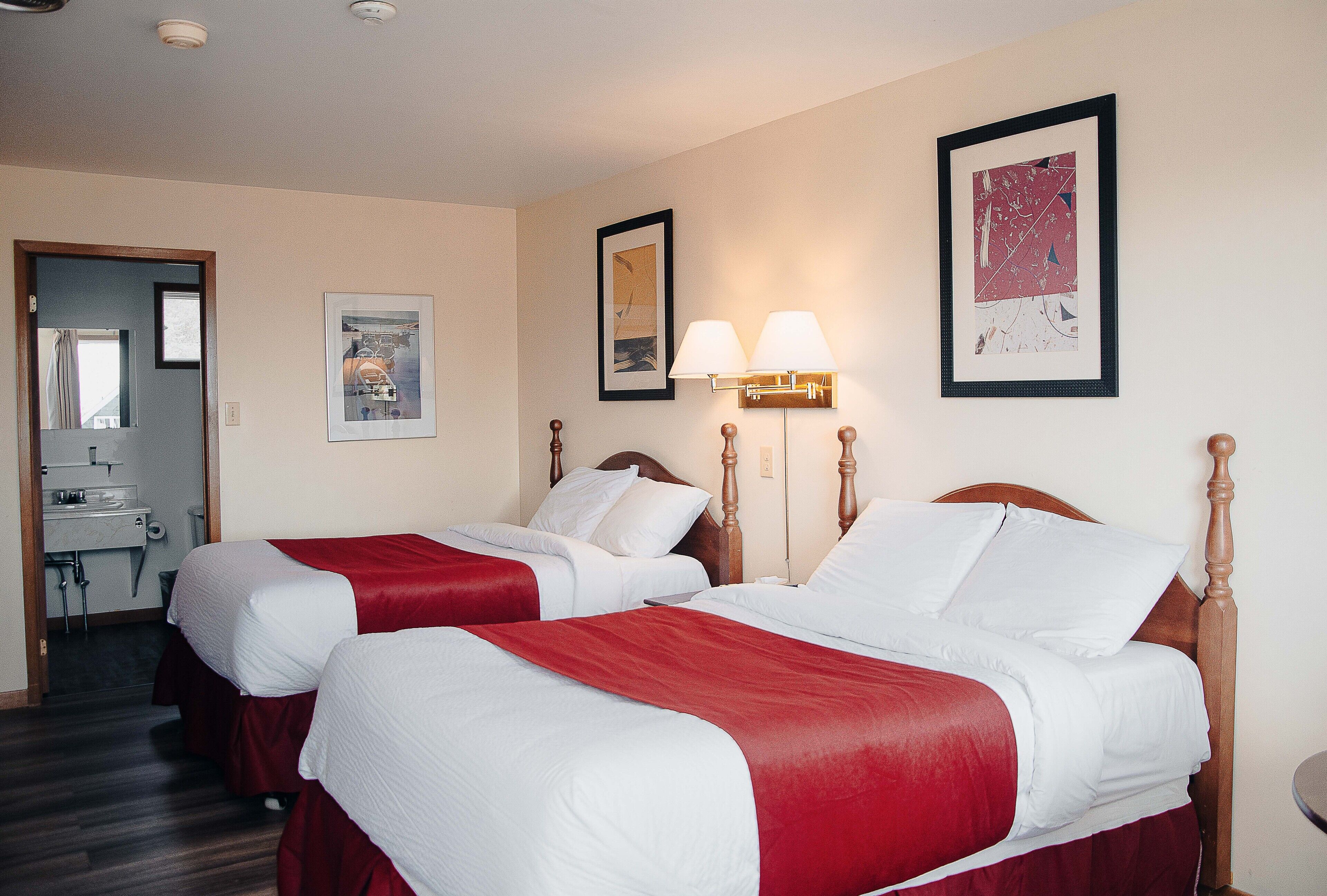 Quarto de hotel com duas camas, banheiro e corredor.