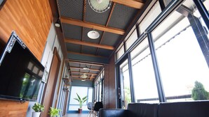Um interior moderno com teto de madeira, janelas amplas, sofá de couro preto e plantas em vasos.
