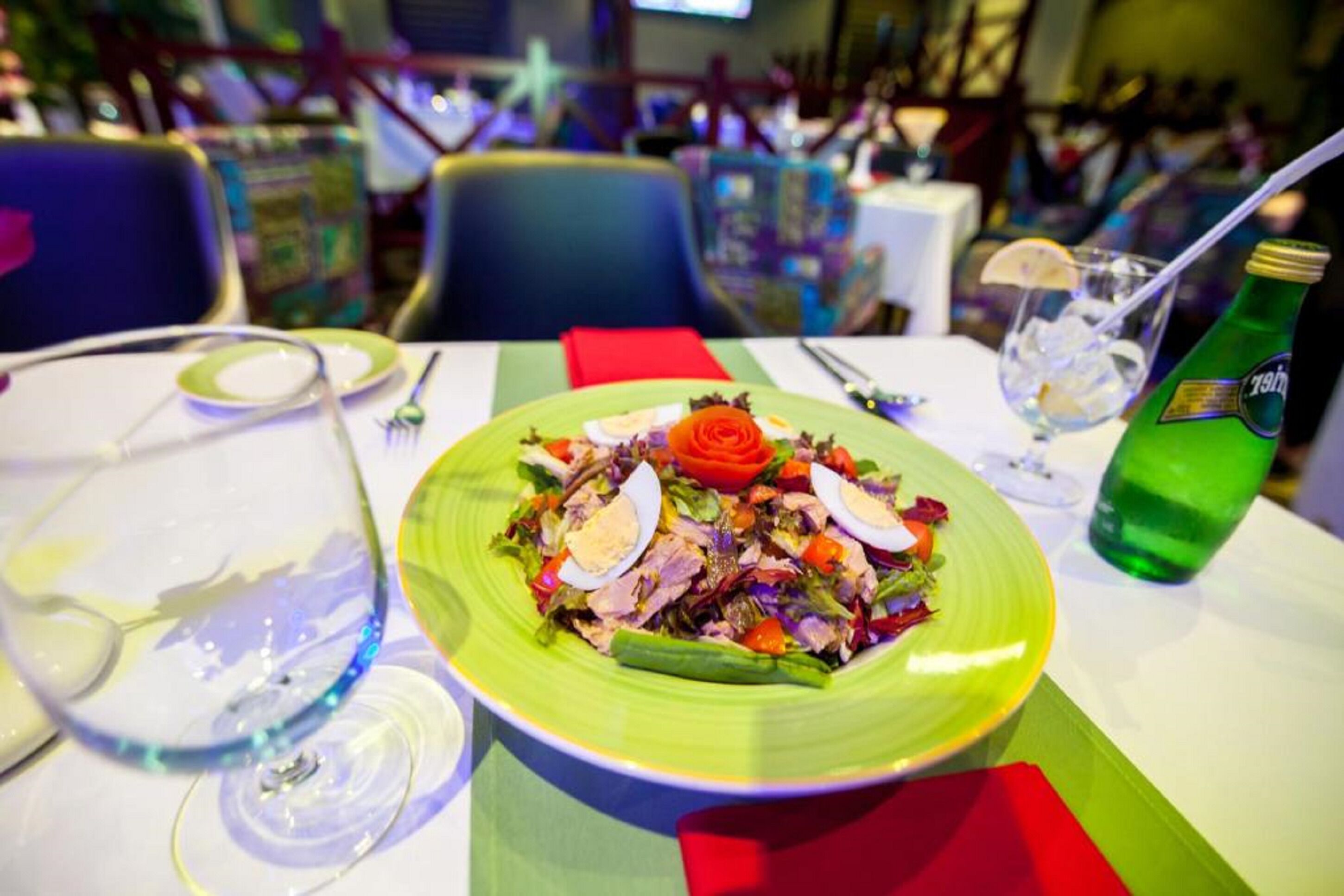 Uma mesa de jantar com um prato de salada verde, um copo de água e uma garrafa de água.