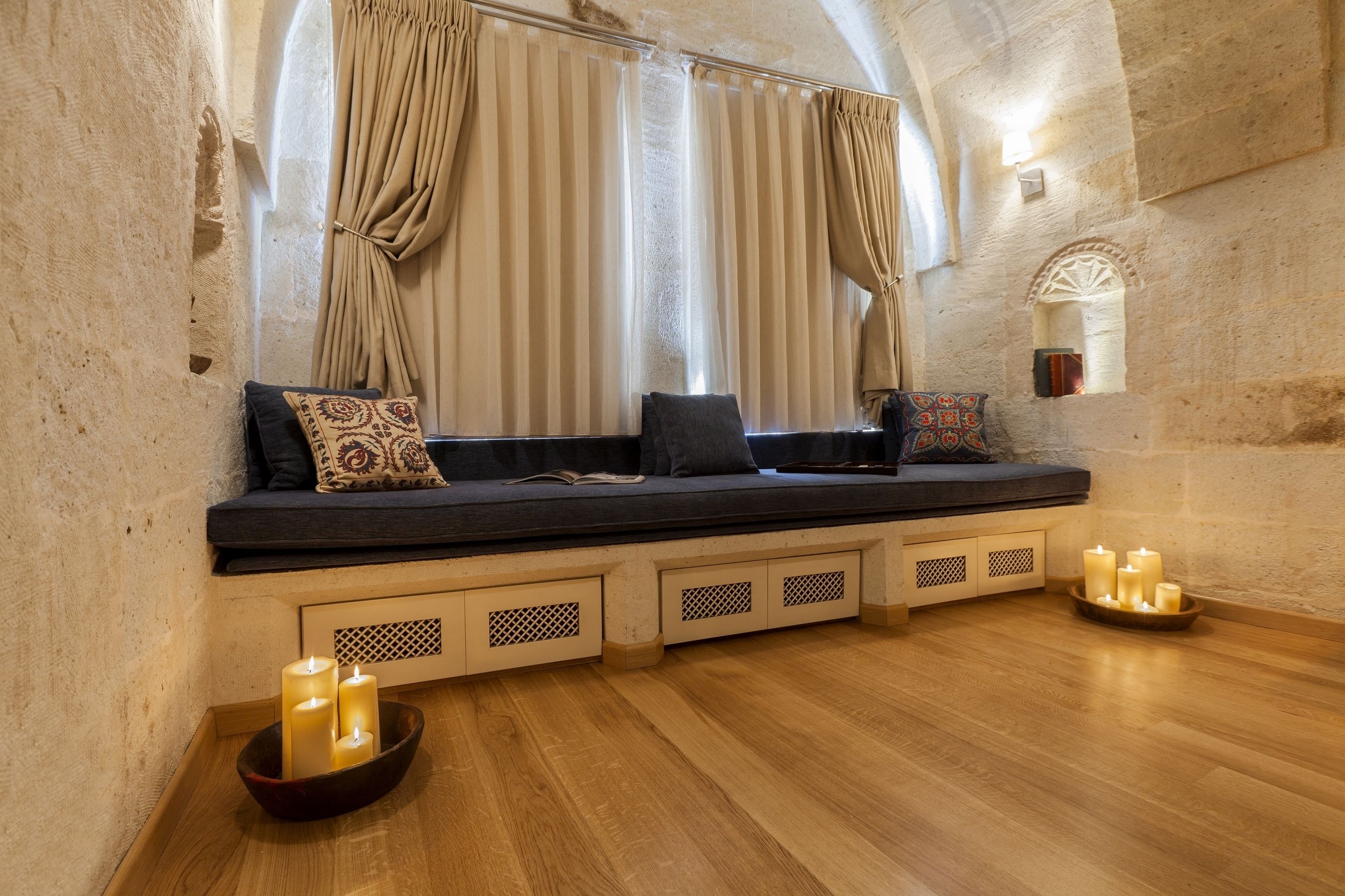Um espaço de estar acolhedor com um banco estofado, uma mesinha com velas e um objeto decorativo na parede.