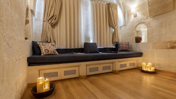 Um espaço de estar acolhedor com um banco estofado, uma mesinha com velas e um objeto decorativo na parede.