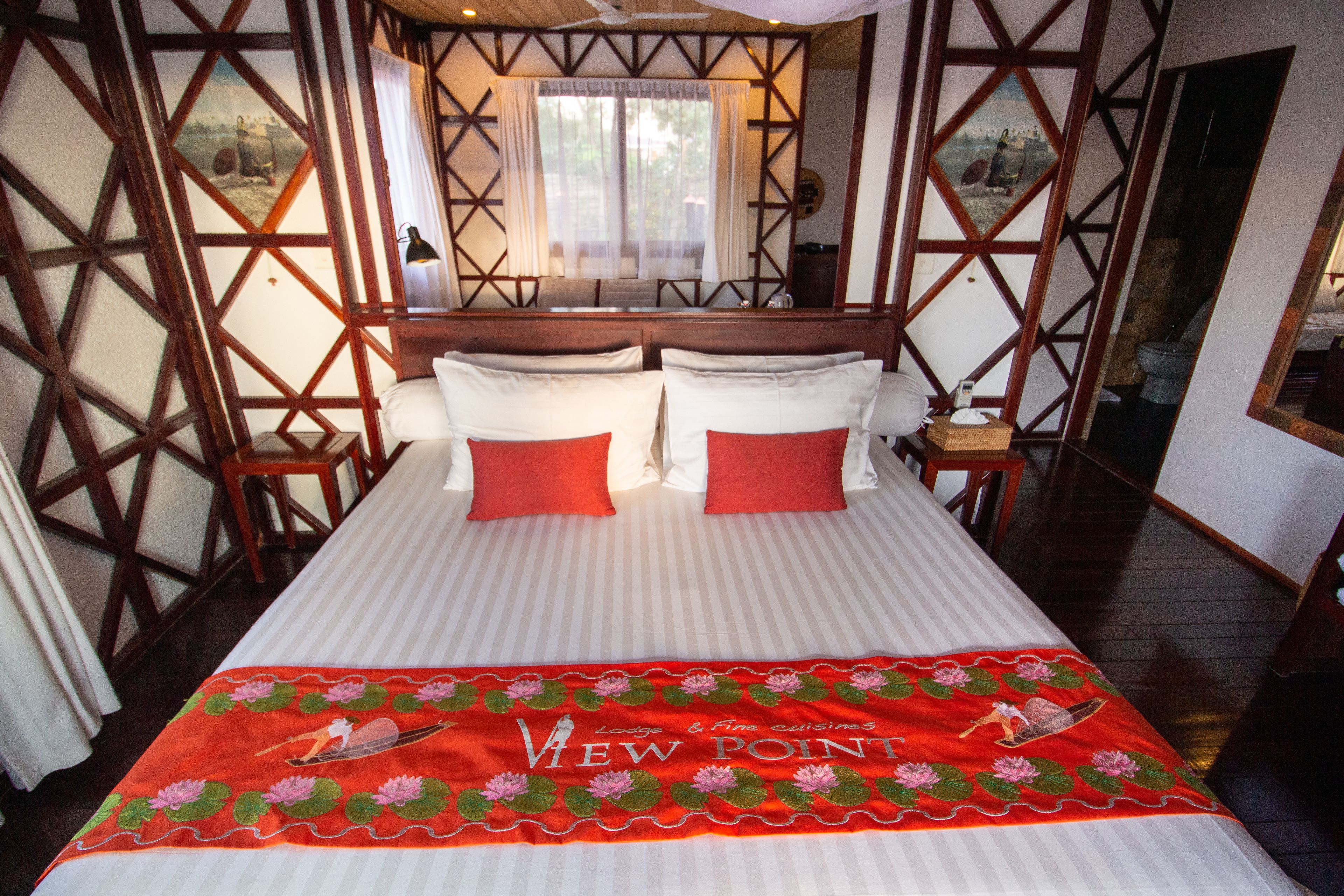 Cama com colcha florida, cabeceira de madeira e duas almofadas vermelhas.