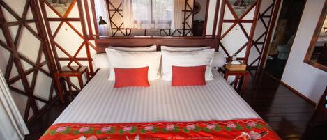 Cama com colcha florida, cabeceira de madeira e duas almofadas vermelhas.