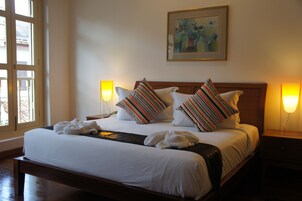 Uma cama bem arrumada com lençóis brancos e almofadas listradas, um abajur e um quadro na parede.