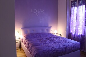 Quarto com cama, projetor fixado na parede exibindo a palavra 'LOVE' e mesa de cabeceira com abajur.