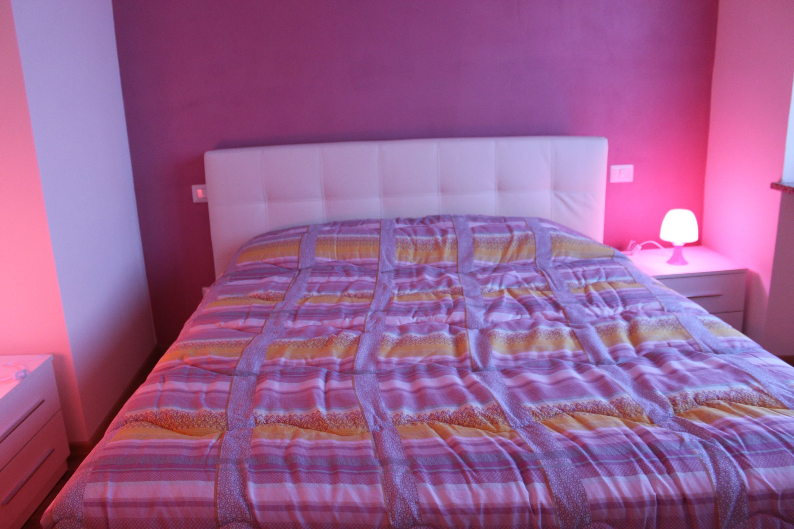 Uma cama com colcha xadrez, cabeceira branca e mesa de cabeceira com abajur.