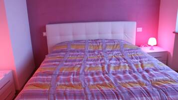 Uma cama com colcha xadrez, cabeceira branca e mesa de cabeceira com abajur.