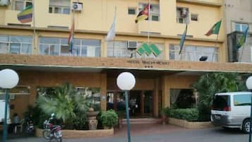 Um hotel com várias bandeiras, fachada de tijolos e área de estacionamento com carros.