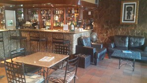 Uma área de bar com parede de pedra, assentos de couro e diversos tipos de bebidas.