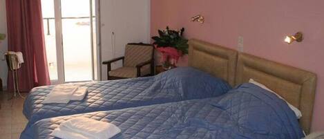 Quarto de hotel com duas camas, uma cadeira, uma planta e um telefone na mesinha de cabeceira.