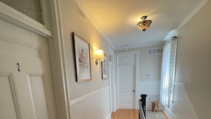 Um corredor com piso de madeira, paredes brancas e escada com corrimão preto.