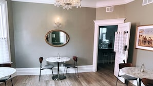 Uma sala de jantar com um candelabro, mesas redondas e cadeiras.