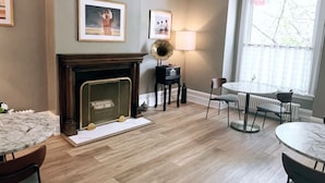 Uma sala de estar com lareira, uma mesa de jantar e uma janela com cortinas.