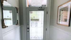 Um corredor com porta branca, tapete preto, radiador e quadro pendurado na parede.