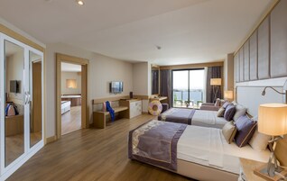 Quarto de hotel com duas camas, uma escrivaninha, uma TV e uma janela grande com vista.