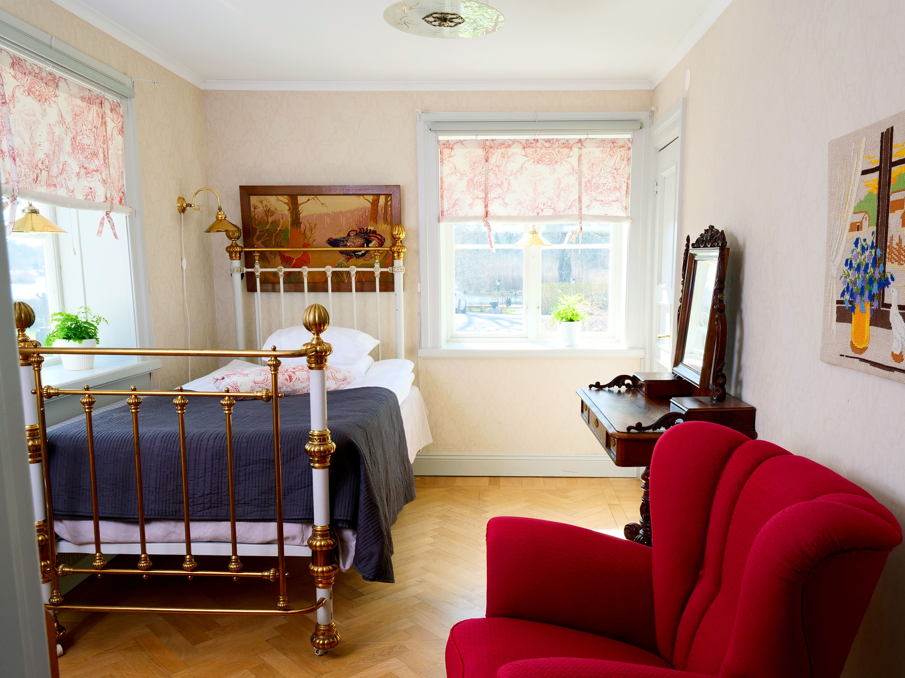 Quarto com uma cama, uma poltrona vermelha, uma cômoda de madeira e um quadro na parede.