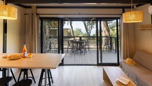 Quarto moderno com mesa de madeira, cadeiras, sofá e uma grande porta de vidro deslizante que dá para uma área externa com mesa e cadeiras.