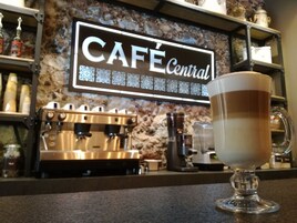 Uma máquina de café e uma xícara de café em uma bancada, com uma placa que diz 'CAFÉ Central' ao fundo.
