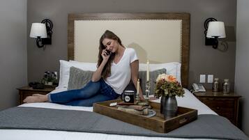 Uma mulher sentada em uma cama com uma bandeja contendo uma vela, uma caneca e um vaso com flores.