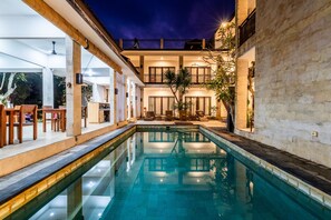Um hotel moderno com piscina central, área de estar externa e estrutura em dois andares com varandas.