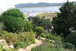 Um jardim com paisagismo e vista para um lago e uma estrada com veículos.