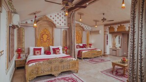 Quarto tradicional com duas camas elaboradas, um ventilador de teto e iluminação decorativa.
