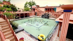 Área de piscina com um padrão geométrico no chão, rodeada por arquitetura tradicional com arcos e uma escadaria que leva a um nível superior.