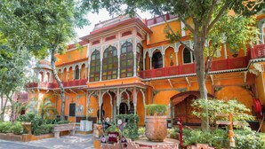 Um edifício tradicional com arquitetura elaborada, grandes janelas e um pátio com plantas em vasos.