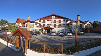 Um hotel com telhado vermelho, chaminés de pedra e um estacionamento com vários carros.