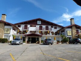 Um edifício de dois andares com entrada central, varandas e estacionamento.