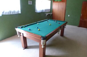 Uma mesa de bilhar com bolas em um salão com paredes verdes e uma porta de madeira.