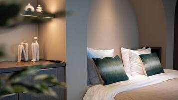 Quarto com cama, almofadas, mesa de cabeceira e prateleira com objetos decorativos.