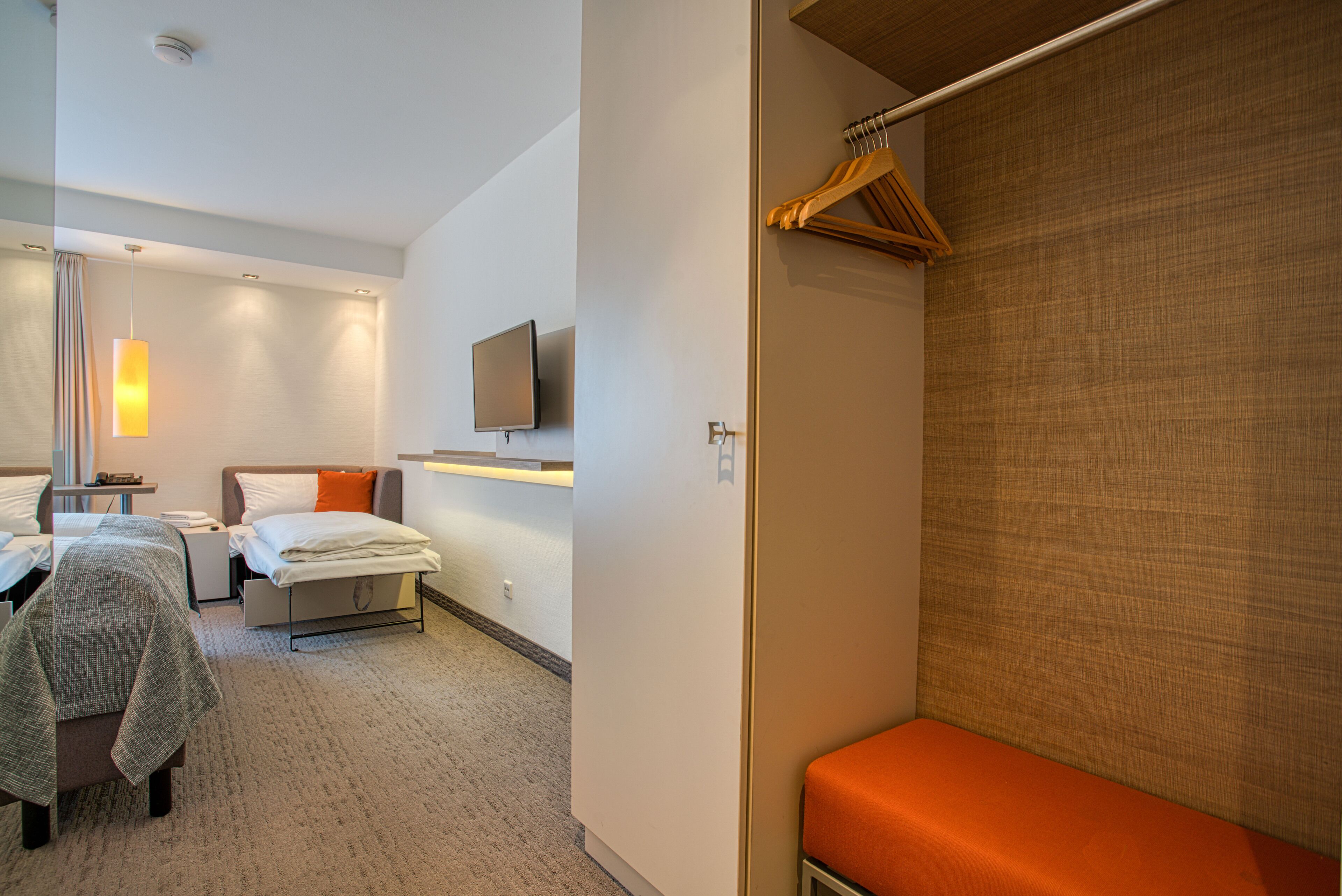 Quarto de hotel com cama, mesa de cabeceira e televisão fixada na parede.
