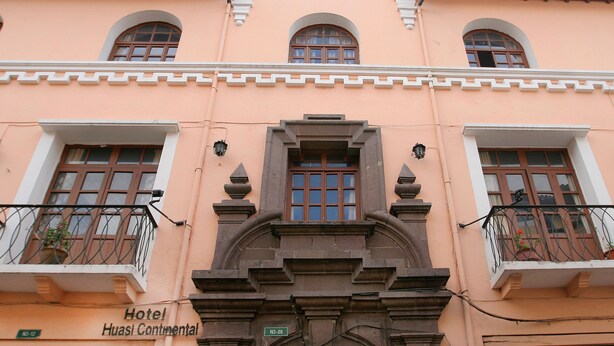 Um edifício com fachada rosa, três janelas em arco e varandas com grades de metal.
