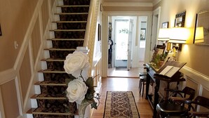 Uma escadaria com carpete estampado, uma mesa com toalha rendada e um vaso de flores brancas.